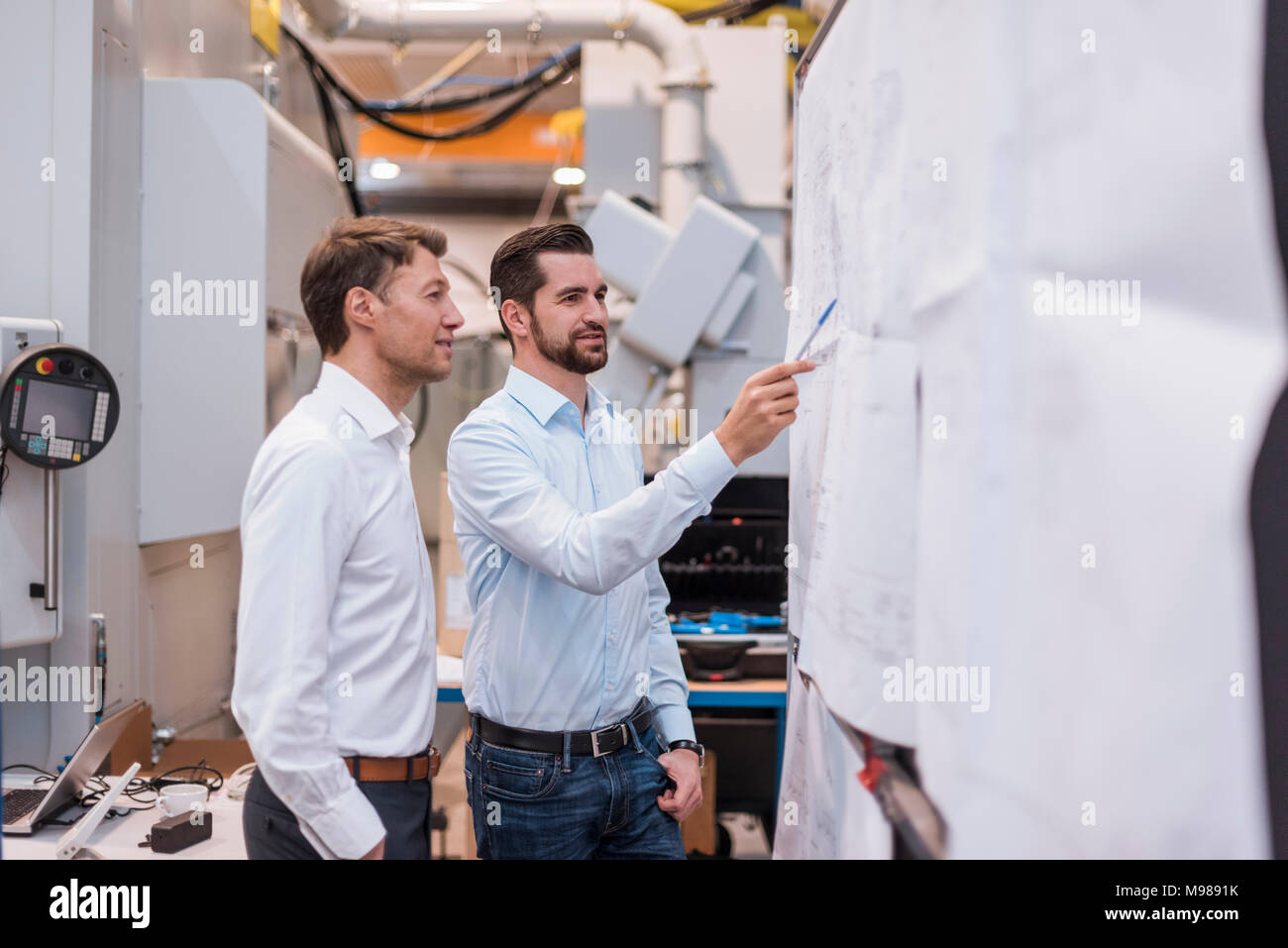 Two men in factory looking at plan Stock Photo - Alamy