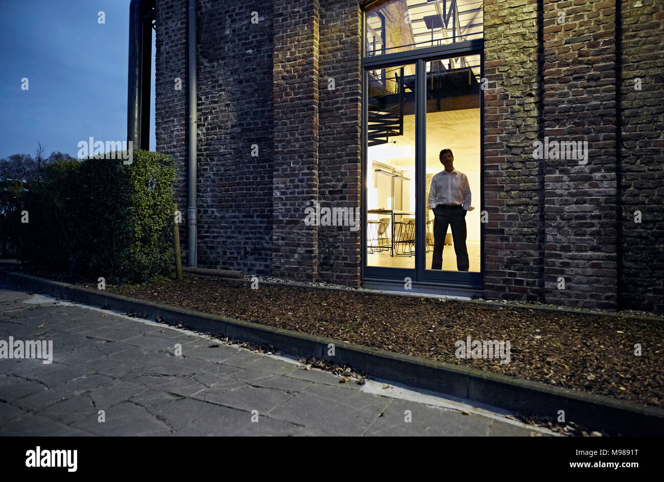 Exterior view of man standing at window of modern building at night ...