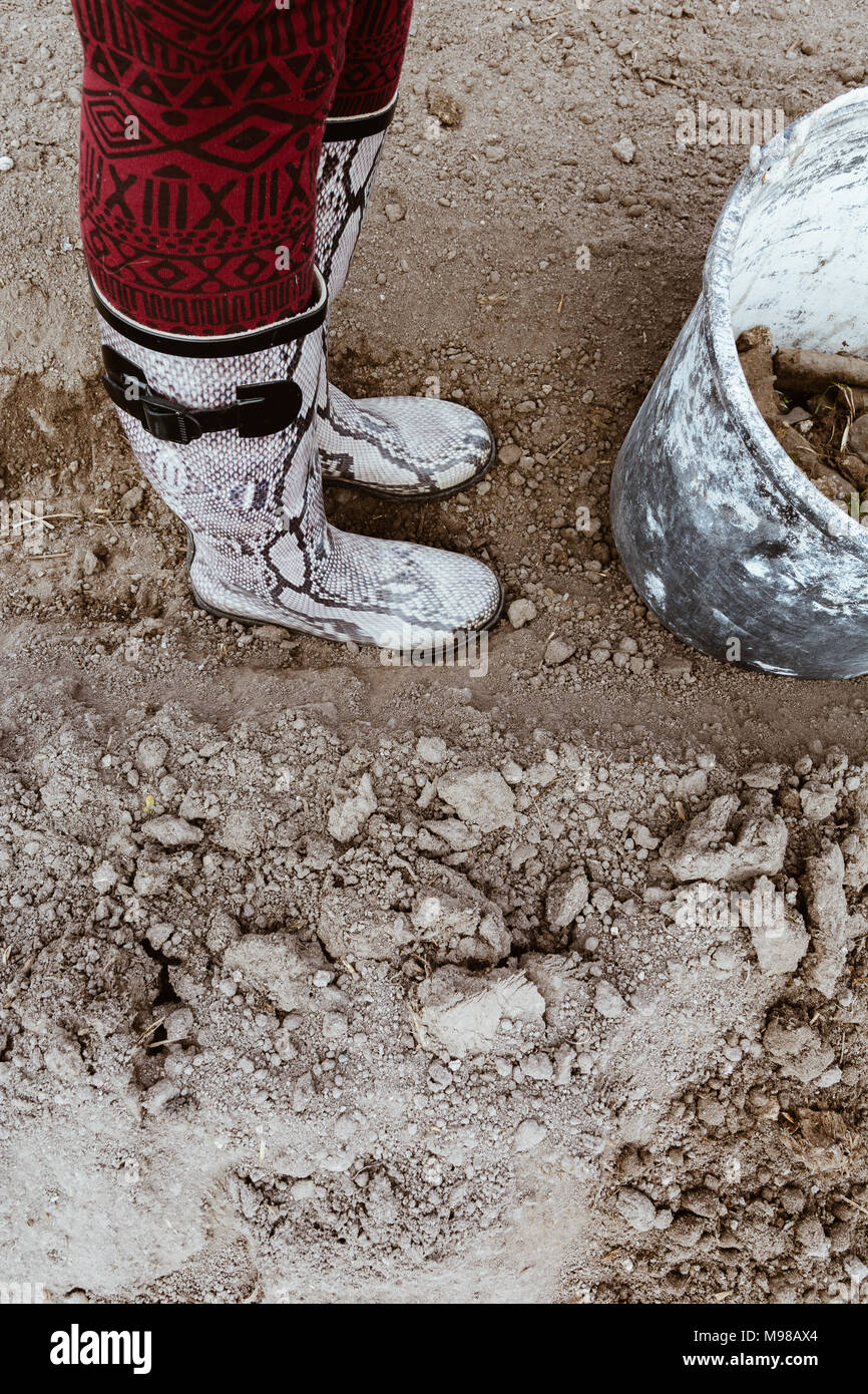 Human legs in rubber boots and old bucket covered in paint with stones ...