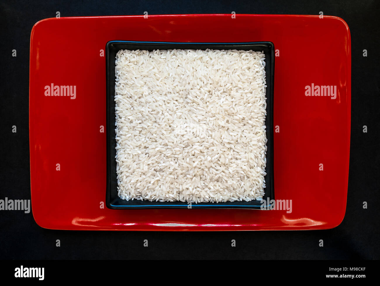 Rice grains in black pate on red plate background surface Stock Photo ...