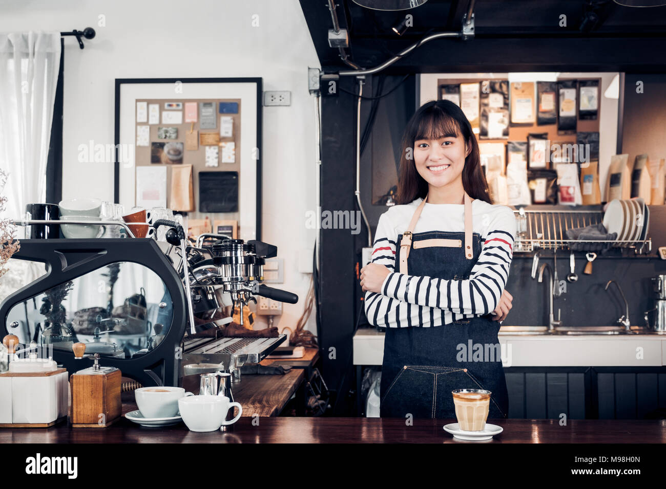 Asian female barista wear jean apron crossed her arms at counter bar ...