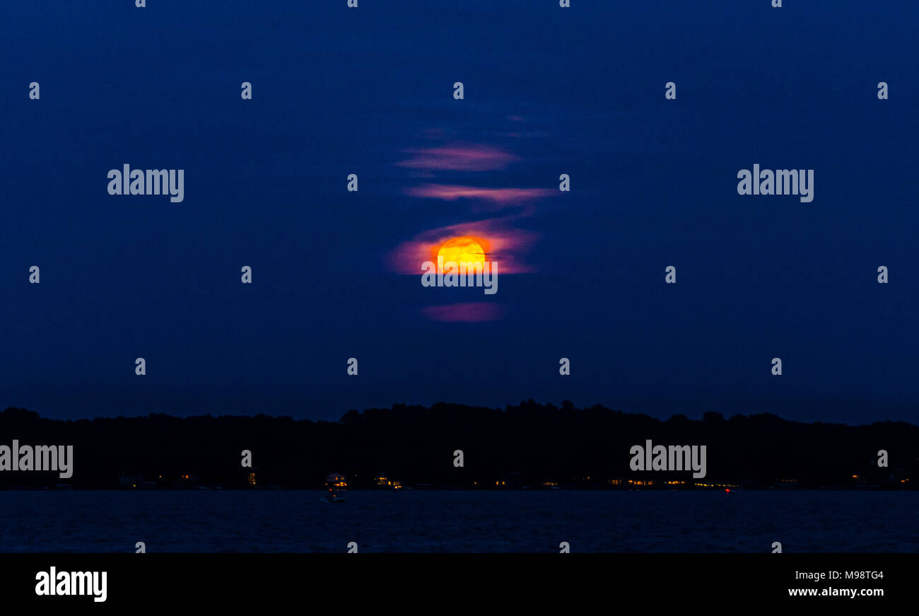 A full moon rises through clouds over Lake Maxinkuckee in Culver ...