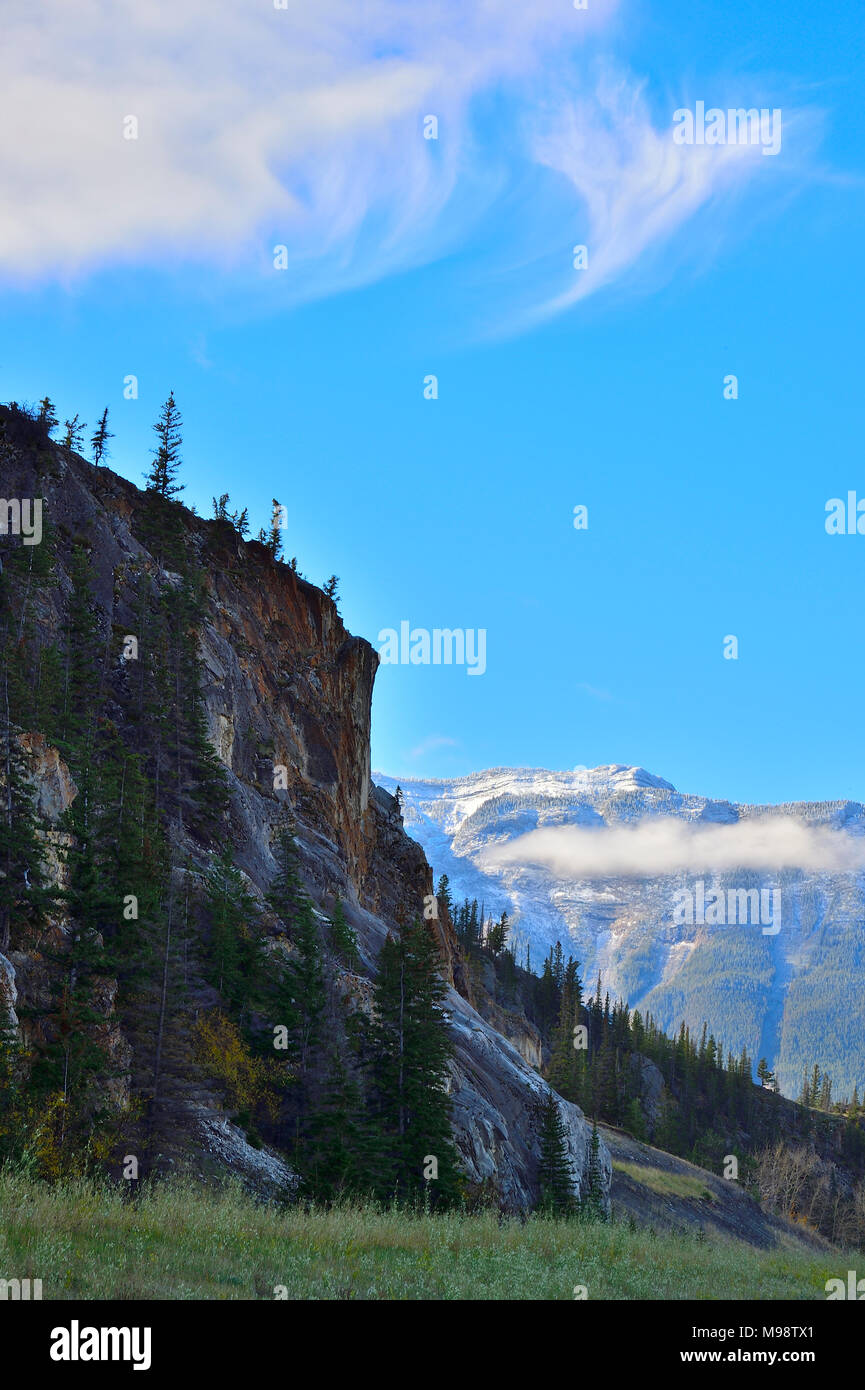 A vertical fall image of a mountain cliff with blue sky and snow-capped ...