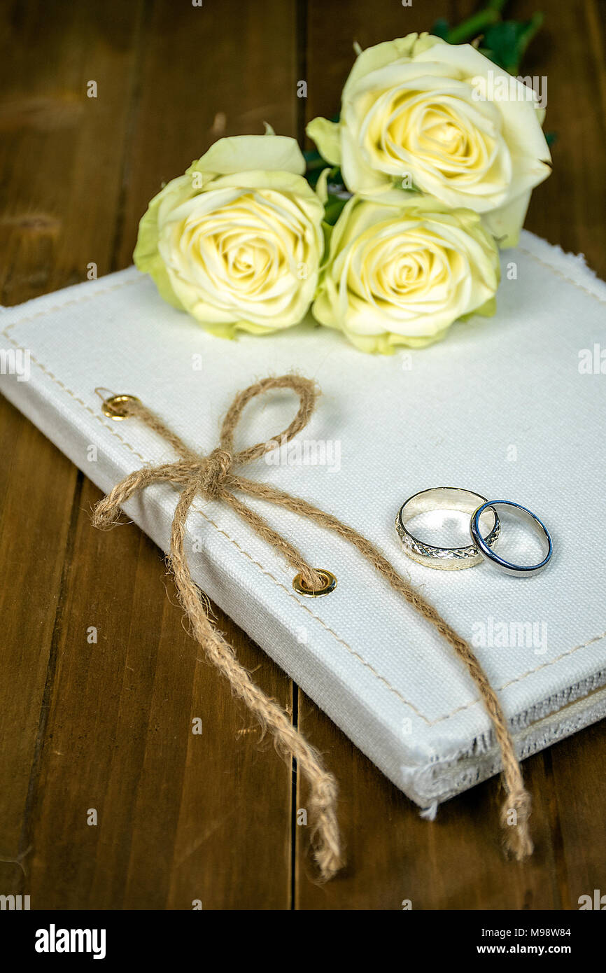 pair of wedding rings on white journal with string bow and rose bouquet ...