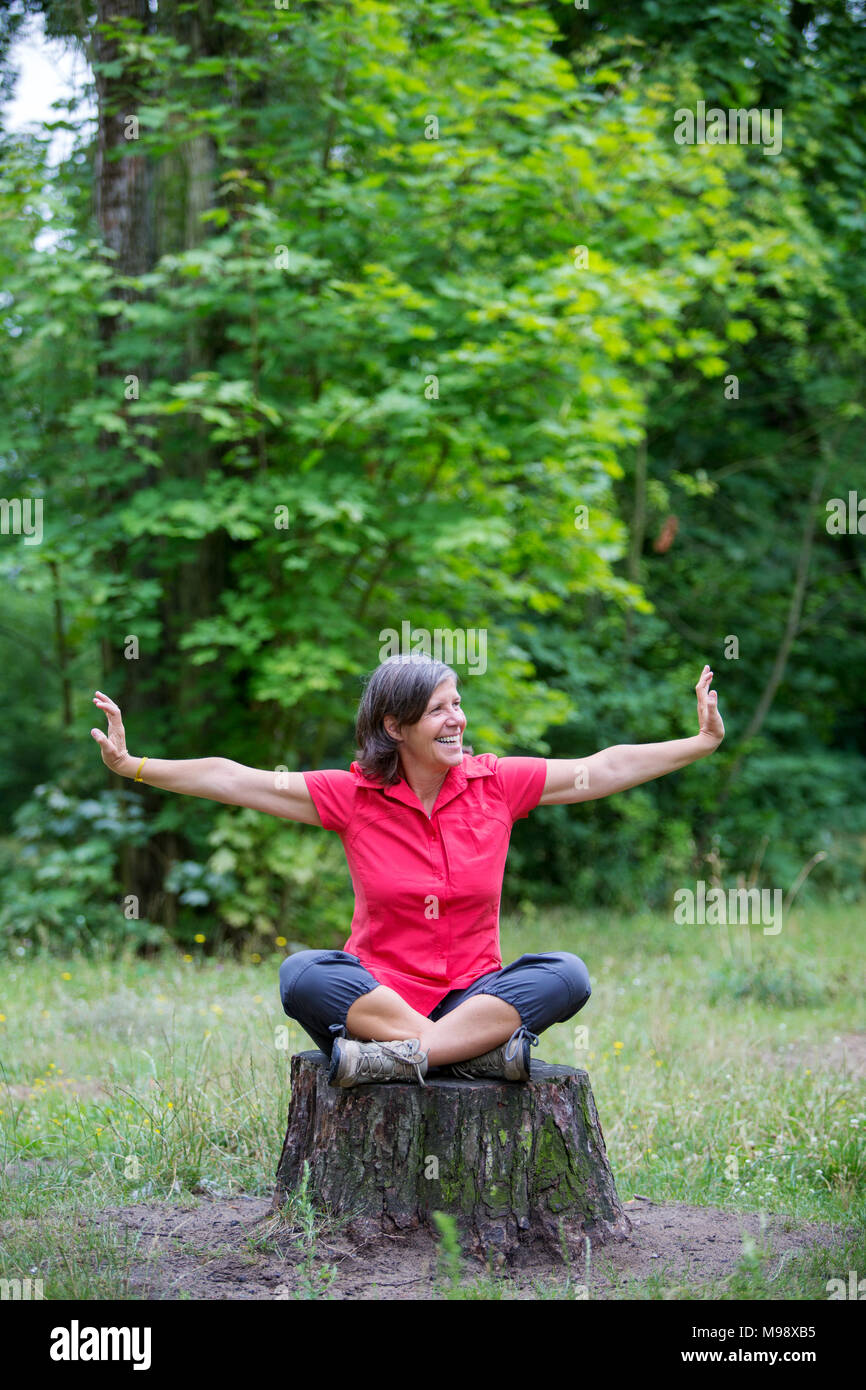 woman in her 50s sitting on a tree stump and is happy Stock Photo - Alamy