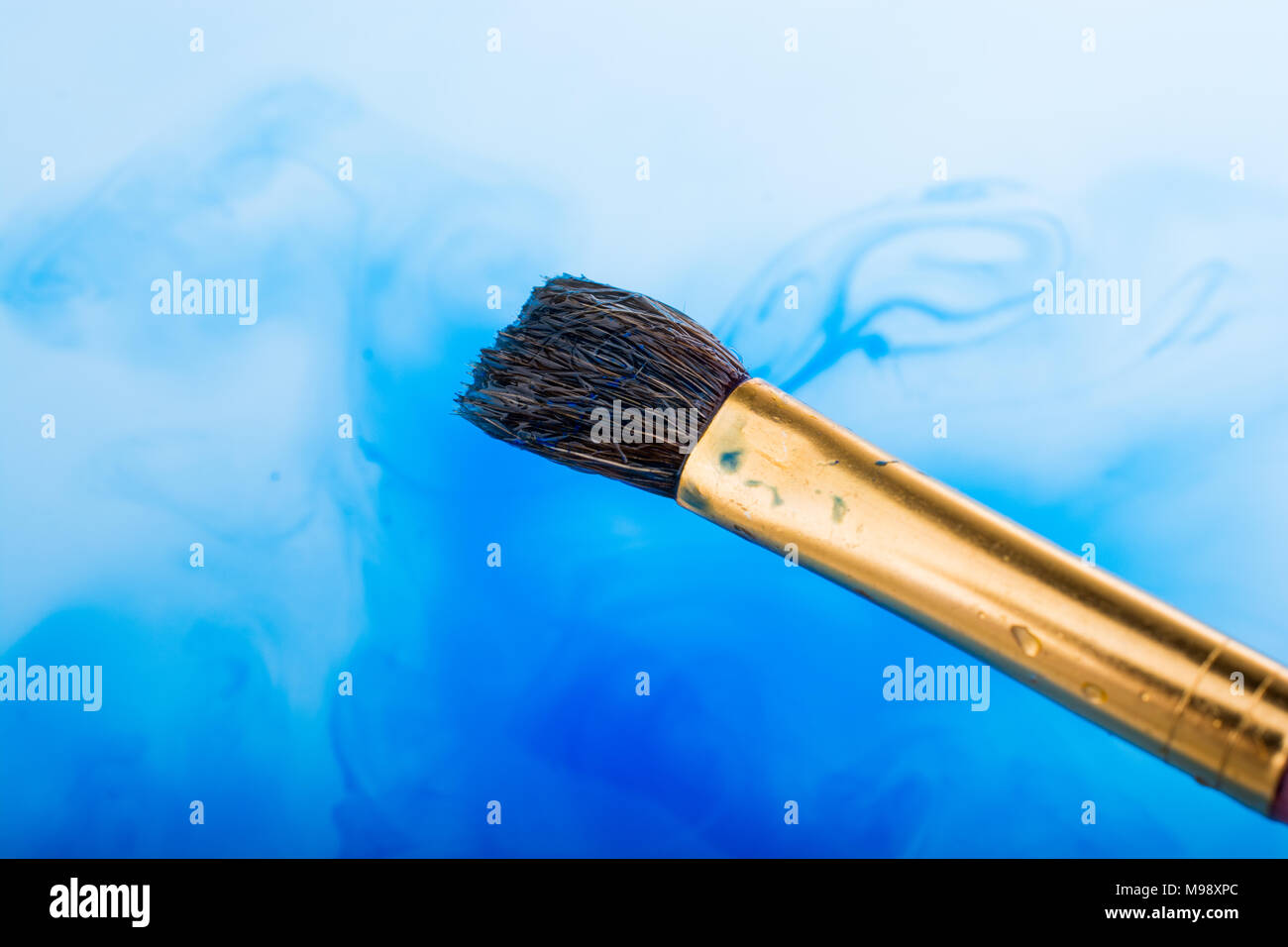 Watercolor paint dissolving in water as painting brush touches water ...