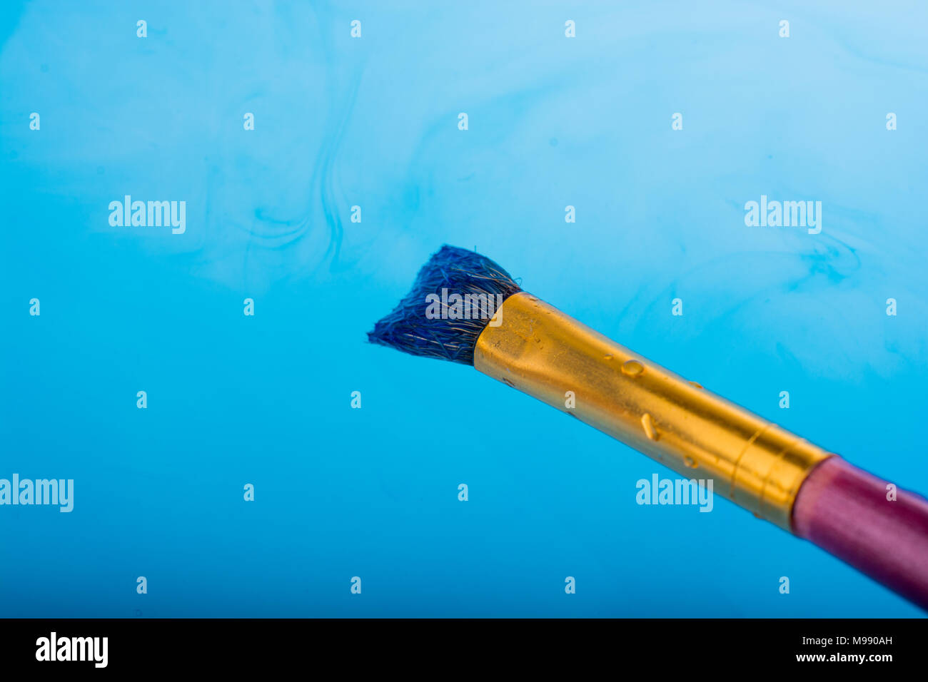 Watercolor paint dissolving in water as painting brush touches water ...