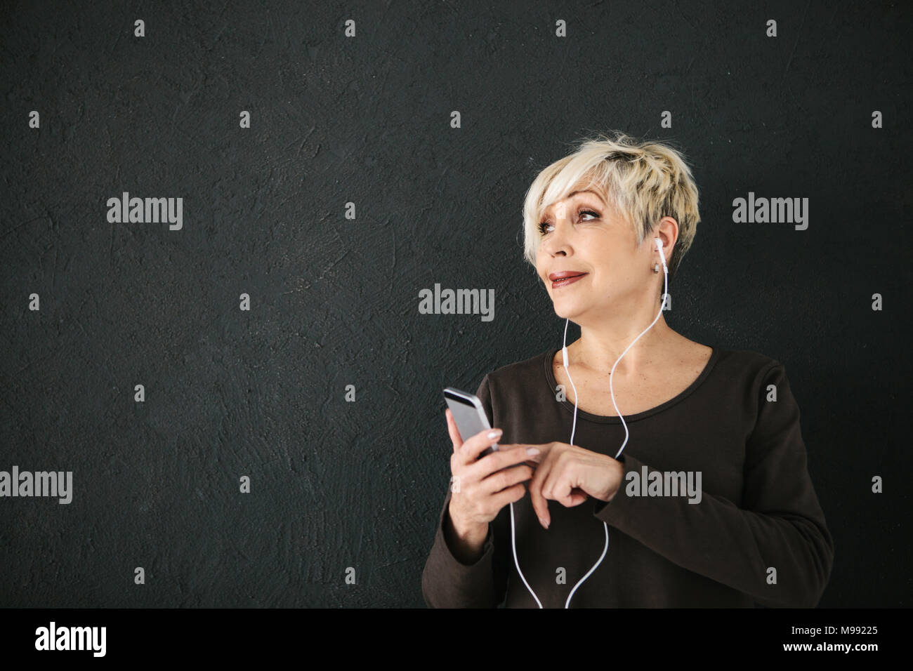 Positive elderly woman listening to music. On a dark background. The ...