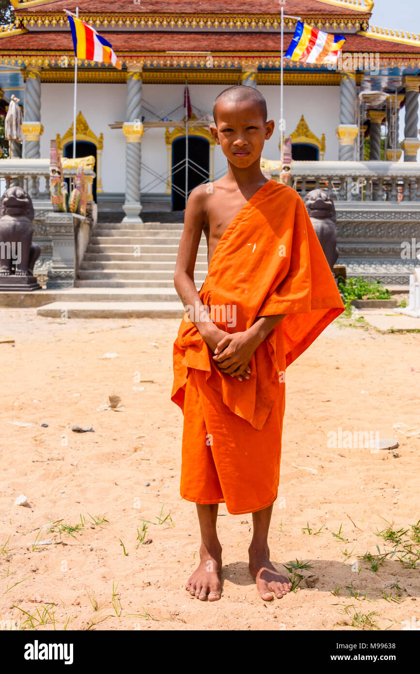A very young boy monk stands outside a Buddhist Temple in a rural area ...