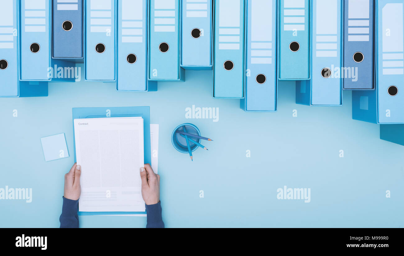 Office worker reading paperwork and archive binders, files database and management concept, top ...