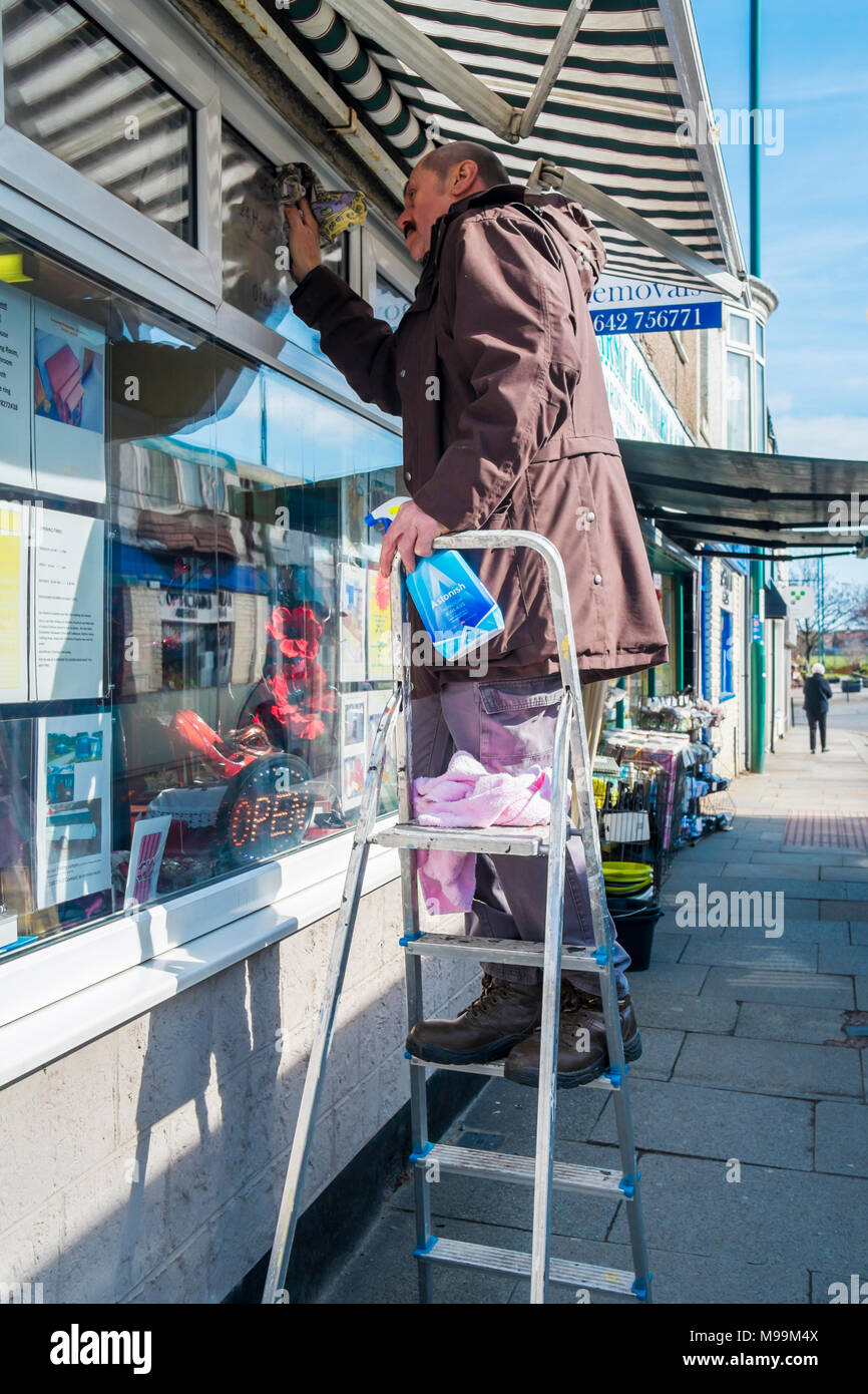 Man on a step ladder cleaning a shop window on a small business in ...