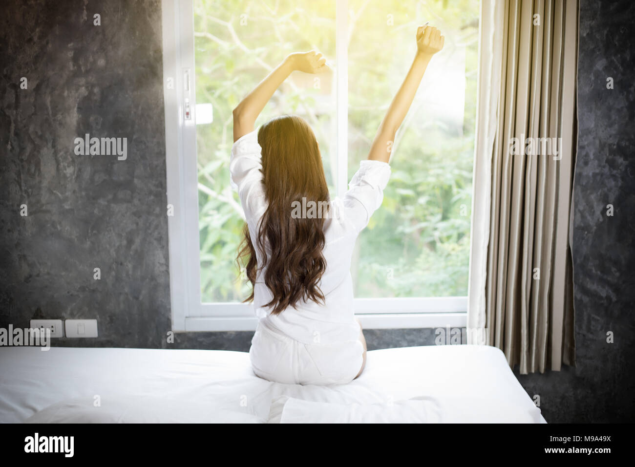 Asian woman Beautiful young smiling woman sitting on bed and stretching ...