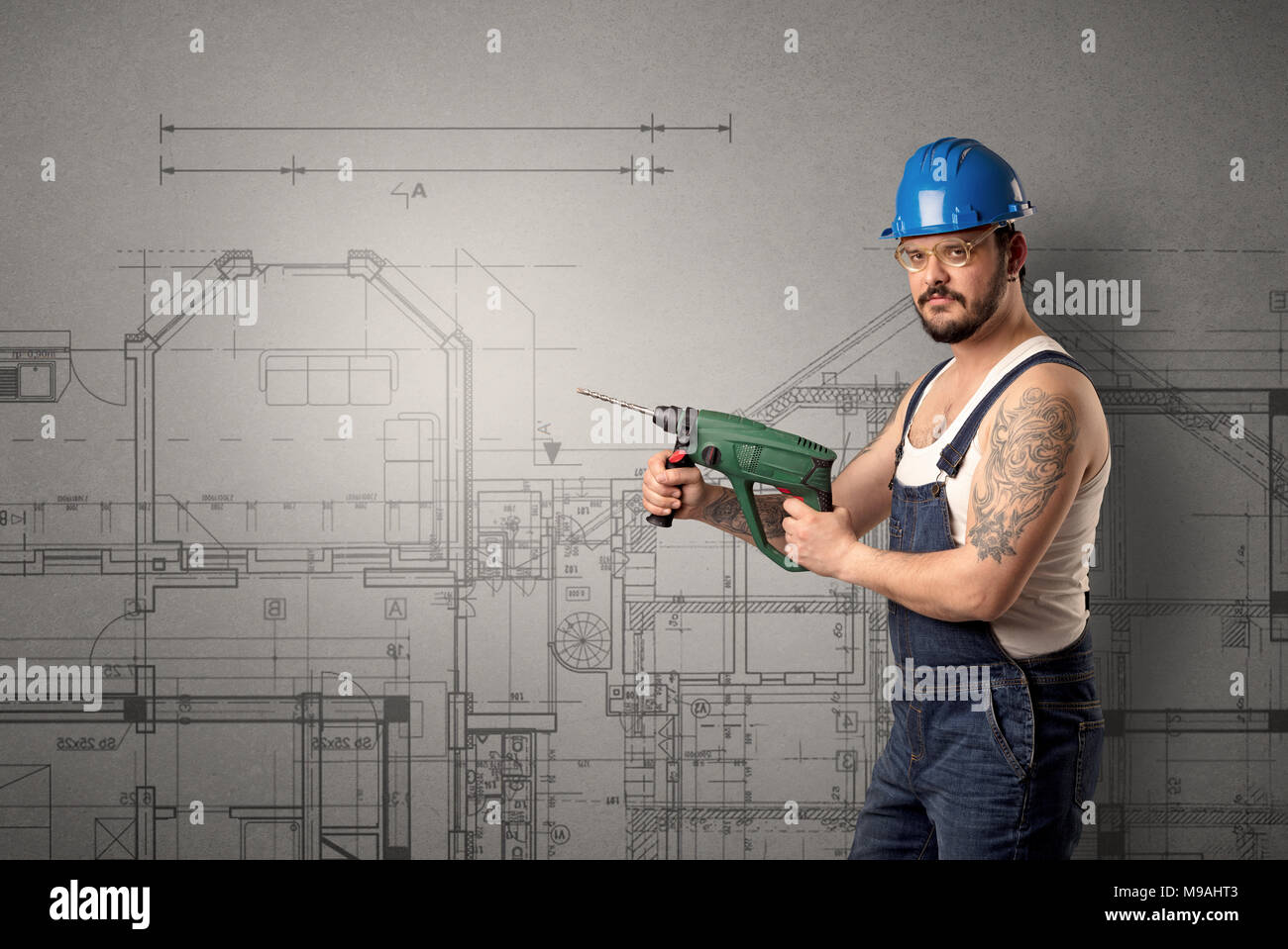 Worker standing with tool in his hand in front of technical drawings ...