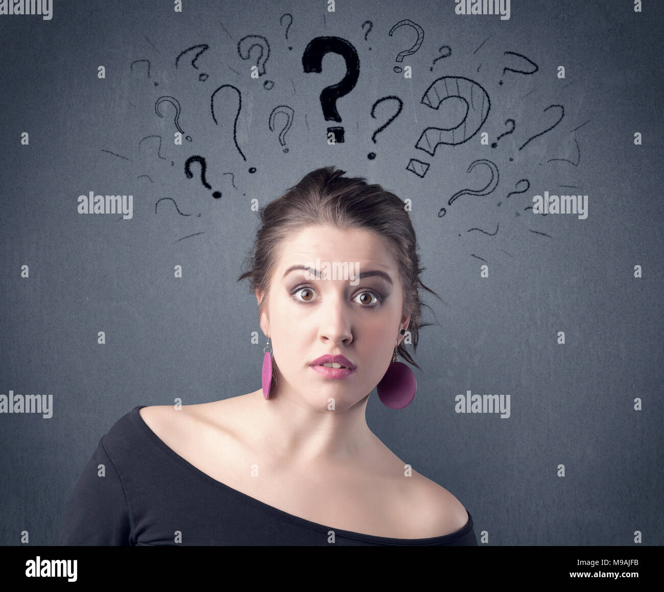 A pretty teenage girl standing confused in front of grey wall ...