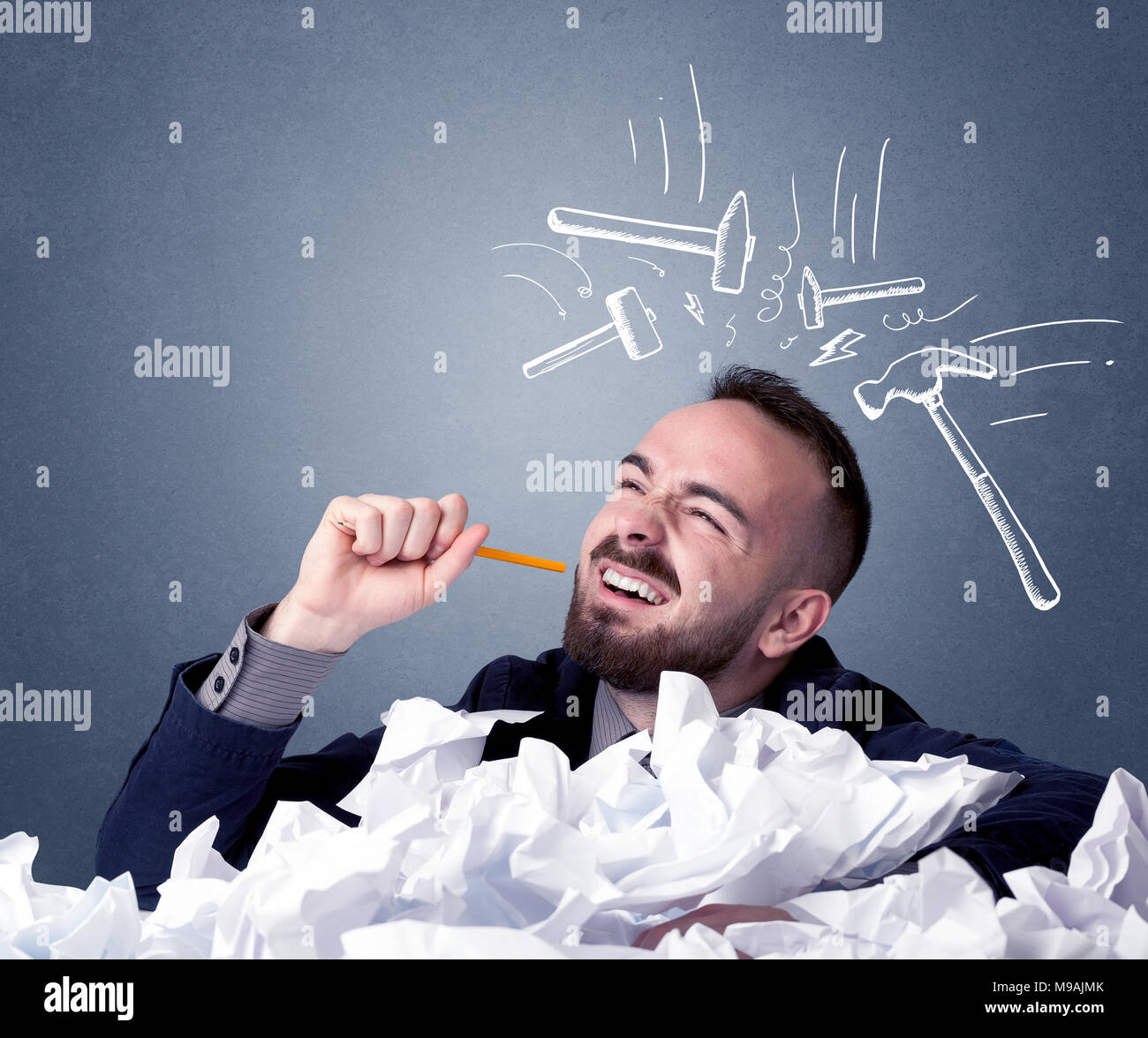 Young businessman sitting behind crumpled paper with drawn hammers ...