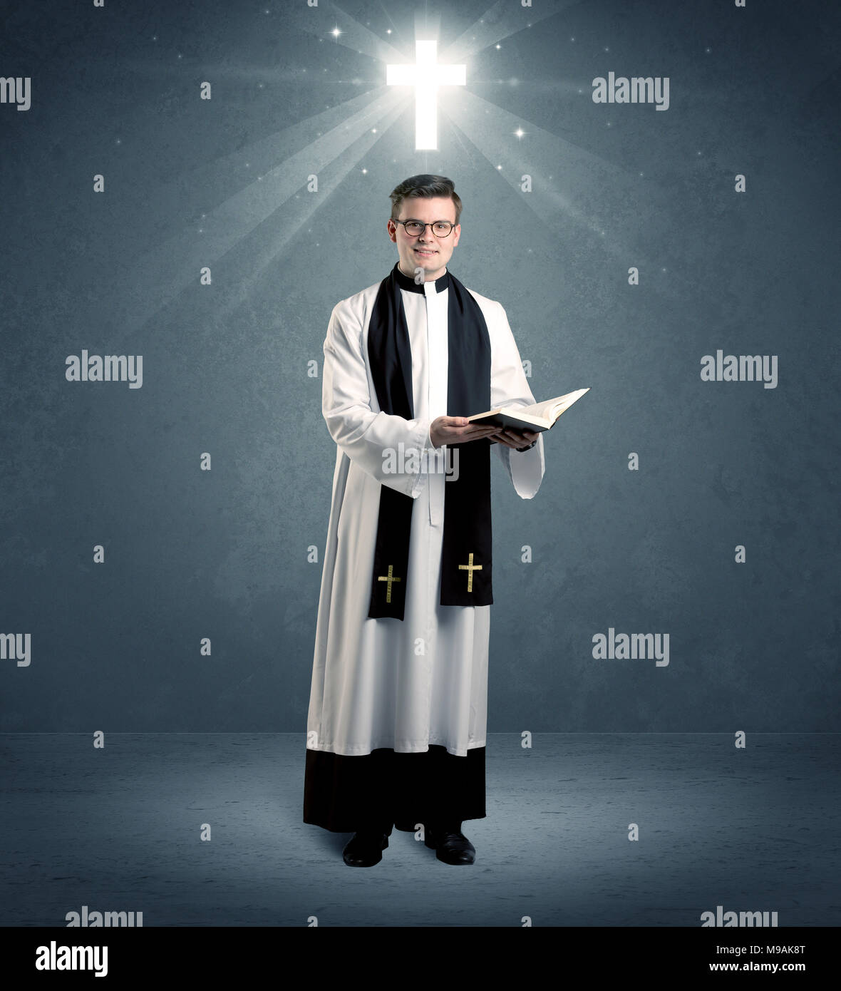 A young caucasian priest with deep faith blessing with the holy bible ...