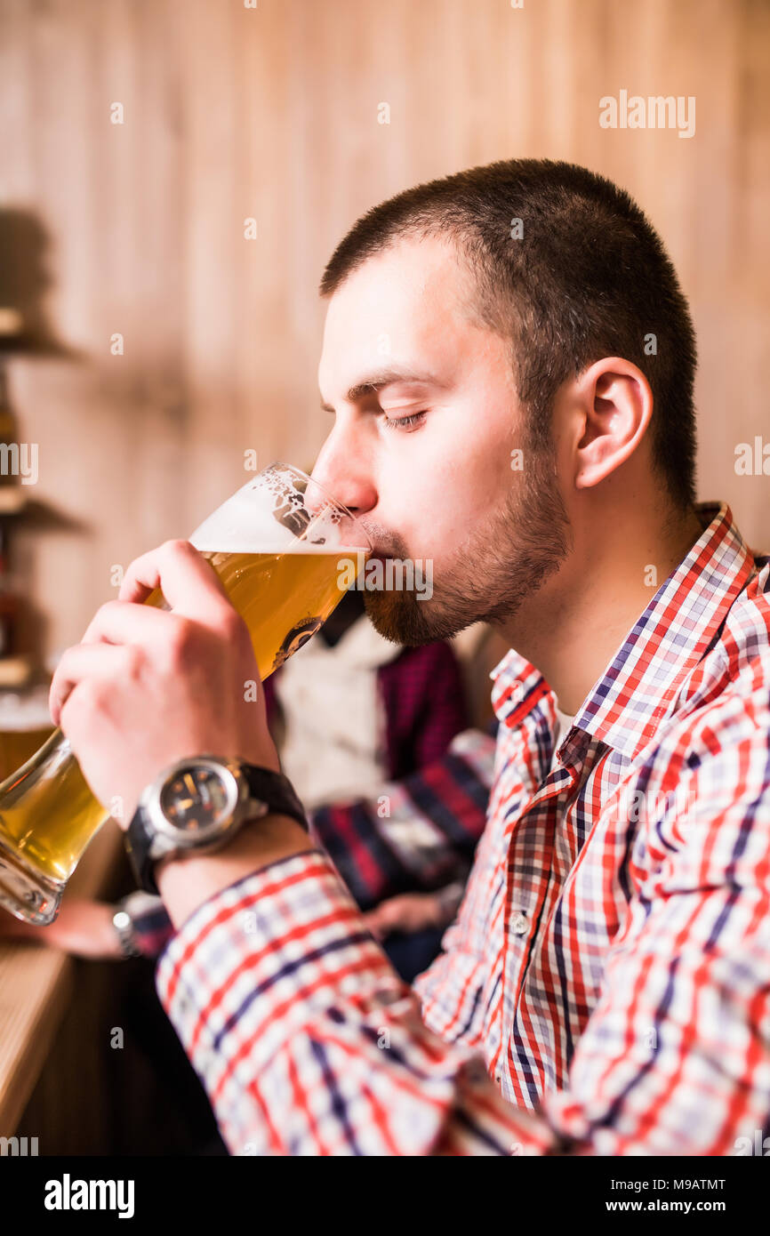 Side view of handsome young man drinking beer while sitting at the bar ...