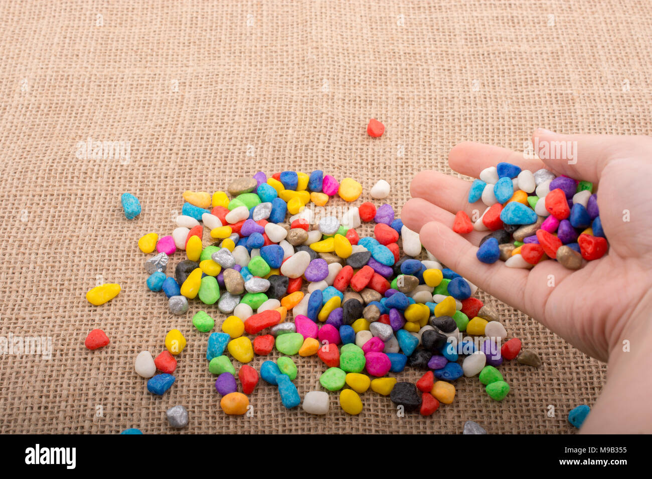 Colorful little pebbles in hand and on canvas ground Stock Photo - Alamy