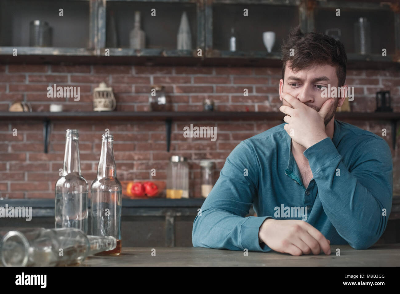 Young man alcohol addiction problems sitting at table looking at empty ...