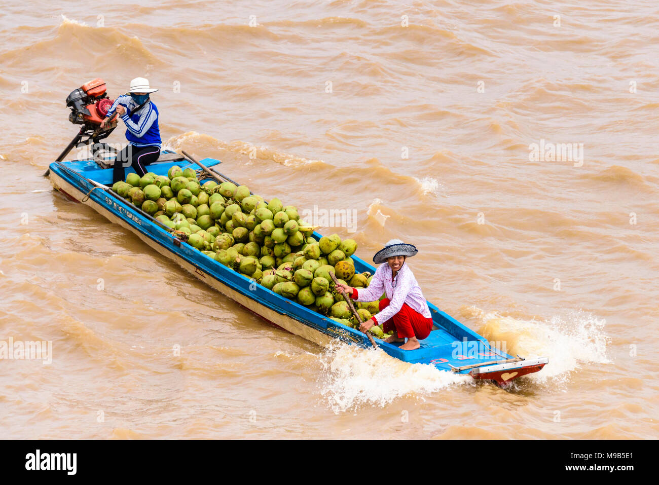 Two Cambodian women bring a cargo of coconuts on a motorboat, Cambodia ...