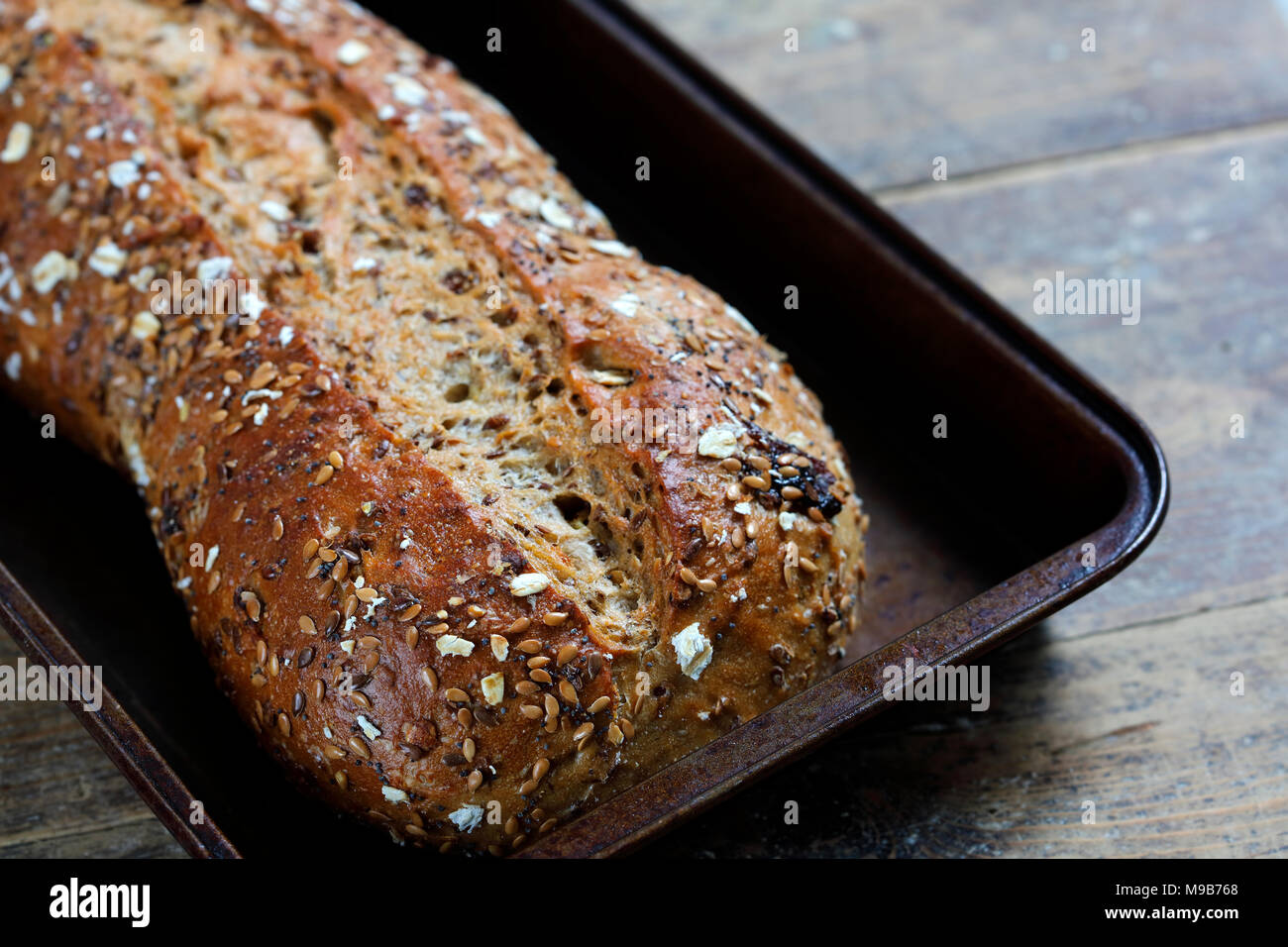 Rustic whole grain bread loaf in baking tray on wooden table Stock ...