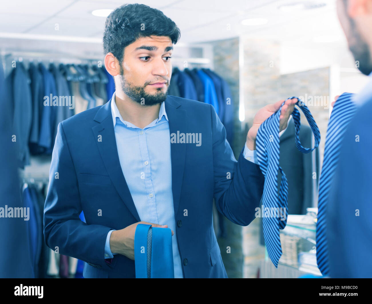 Smiling man is picking up tie for jacket in front of the mirror in men ...
