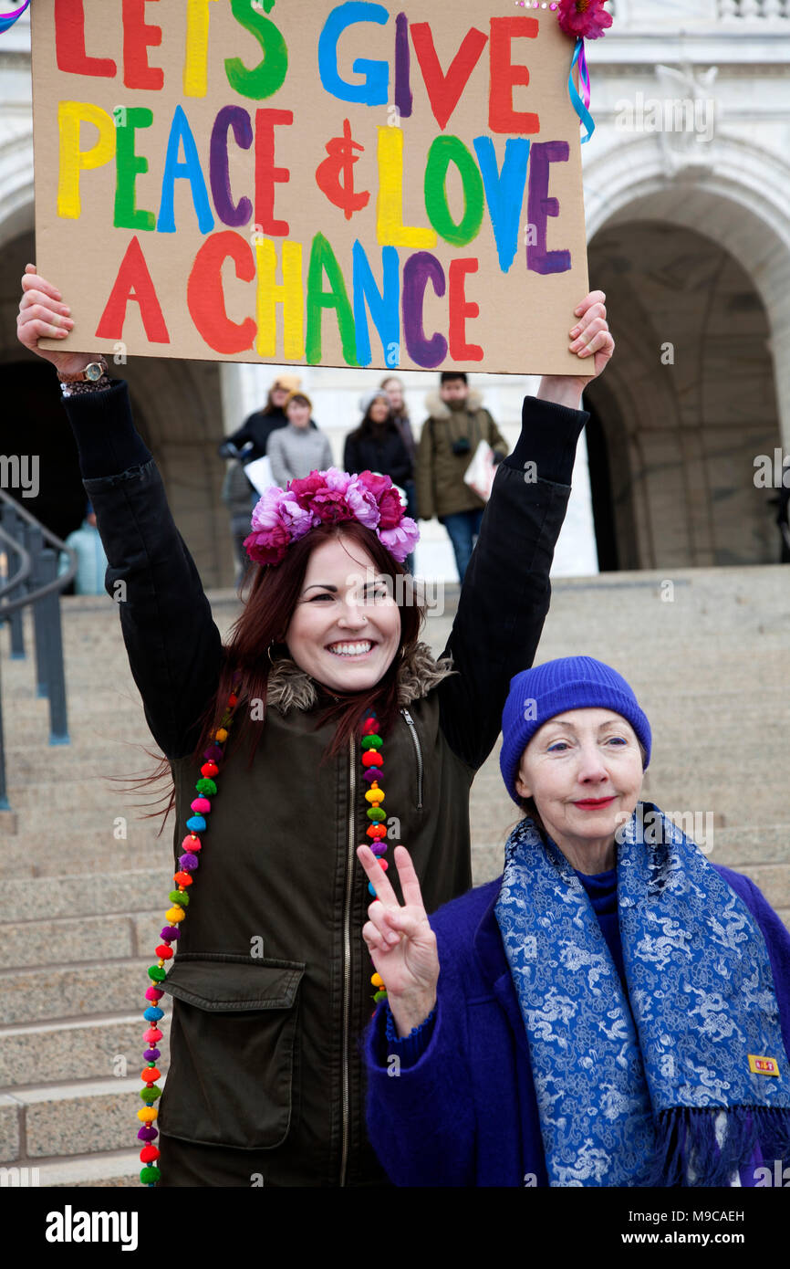 Woman activist giving the peace symbol with student holding "Lets give ...