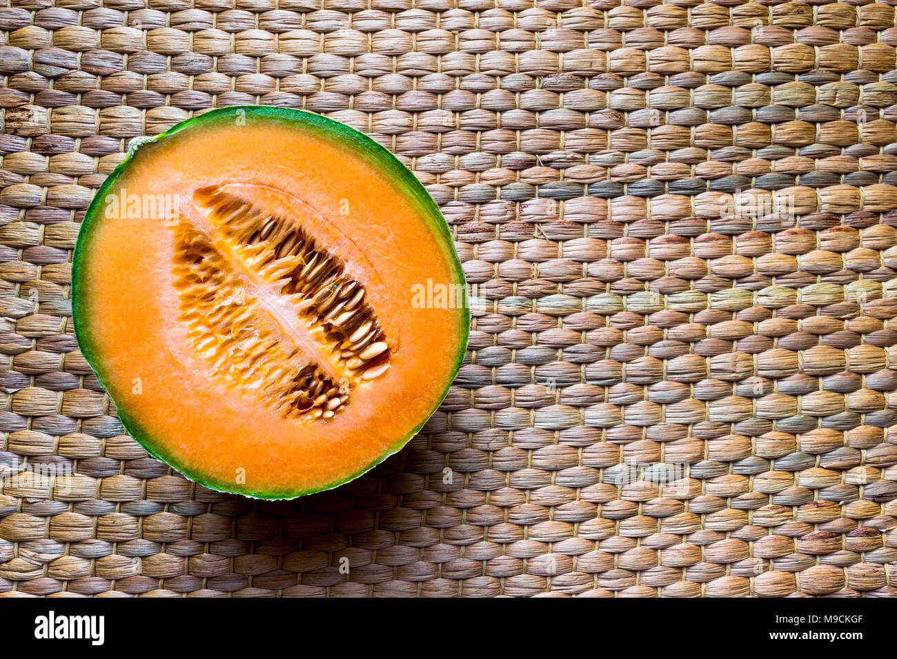 Cut ted in the half Hami melon fruit placed on brown straw mat ...