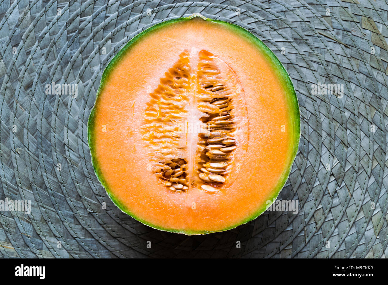 Cut ted in the half of Hami melon fruit on green straw mat background ...