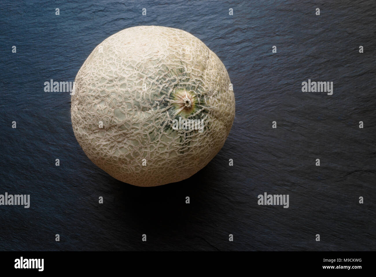 Full head of Hami melon fruit on black stone surface background with ...