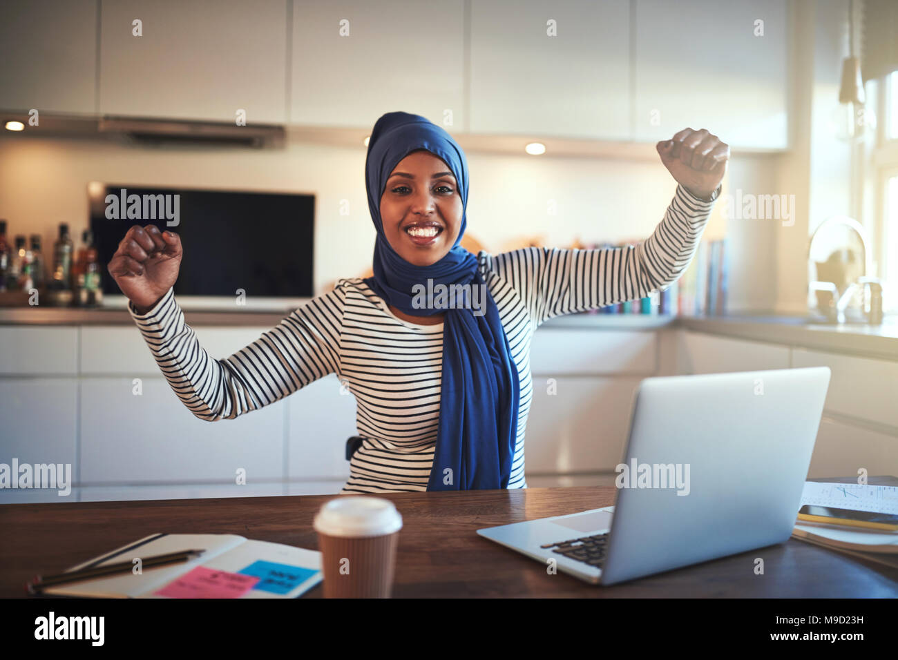 Ecstatic young Muslim female entrepreneur wearing a hijab raising her ...