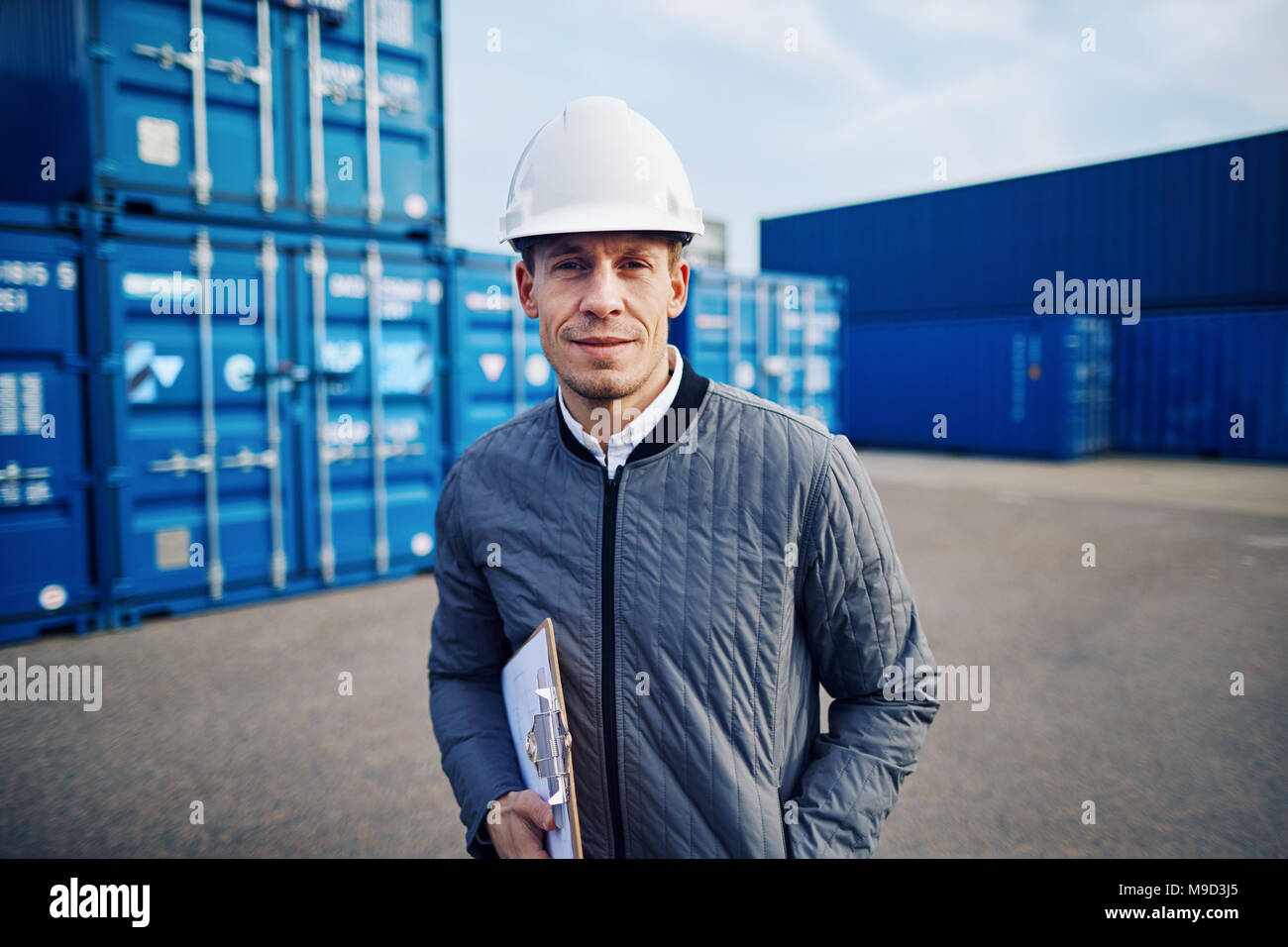 Smiling dock foreman wearing a hardhat standing alone in a large ...