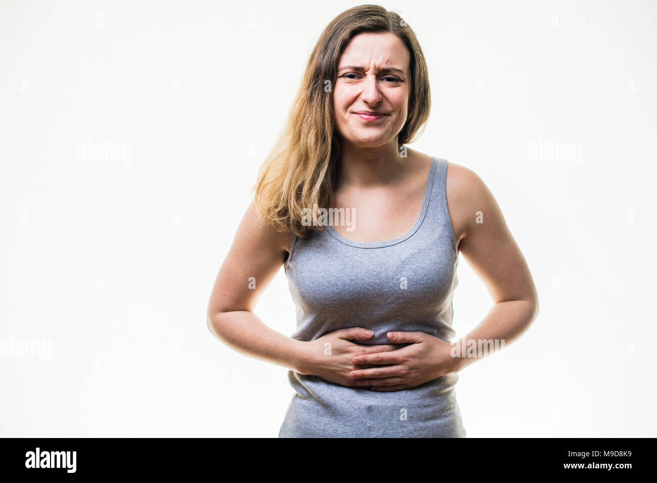 A young Caucasian woman girl wearing a grey vest, rubbing heer stomach ...