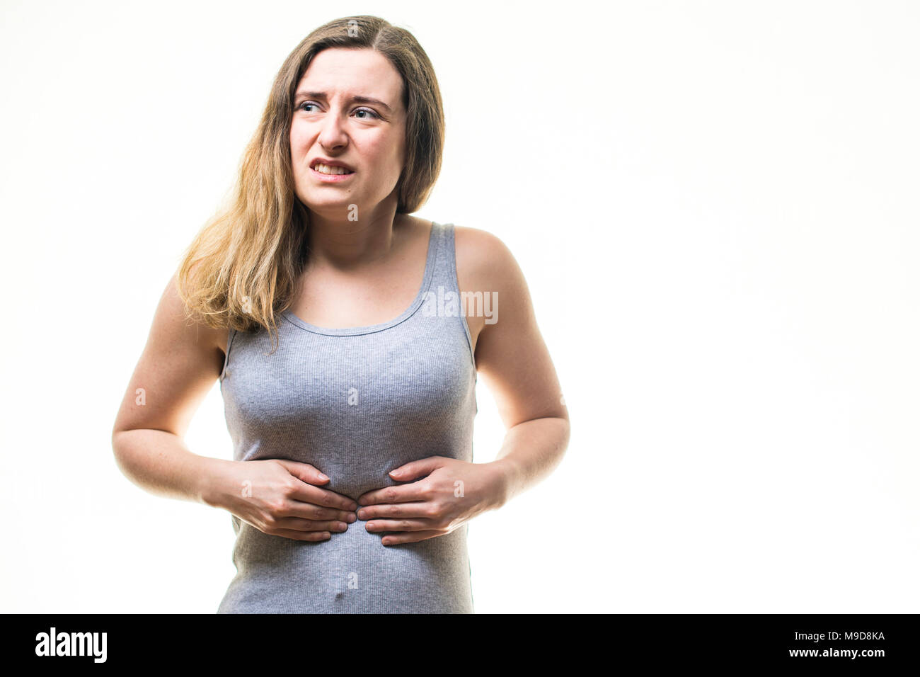 A young Caucasian woman girl wearing a grey vest, rubbing heer stomach ...