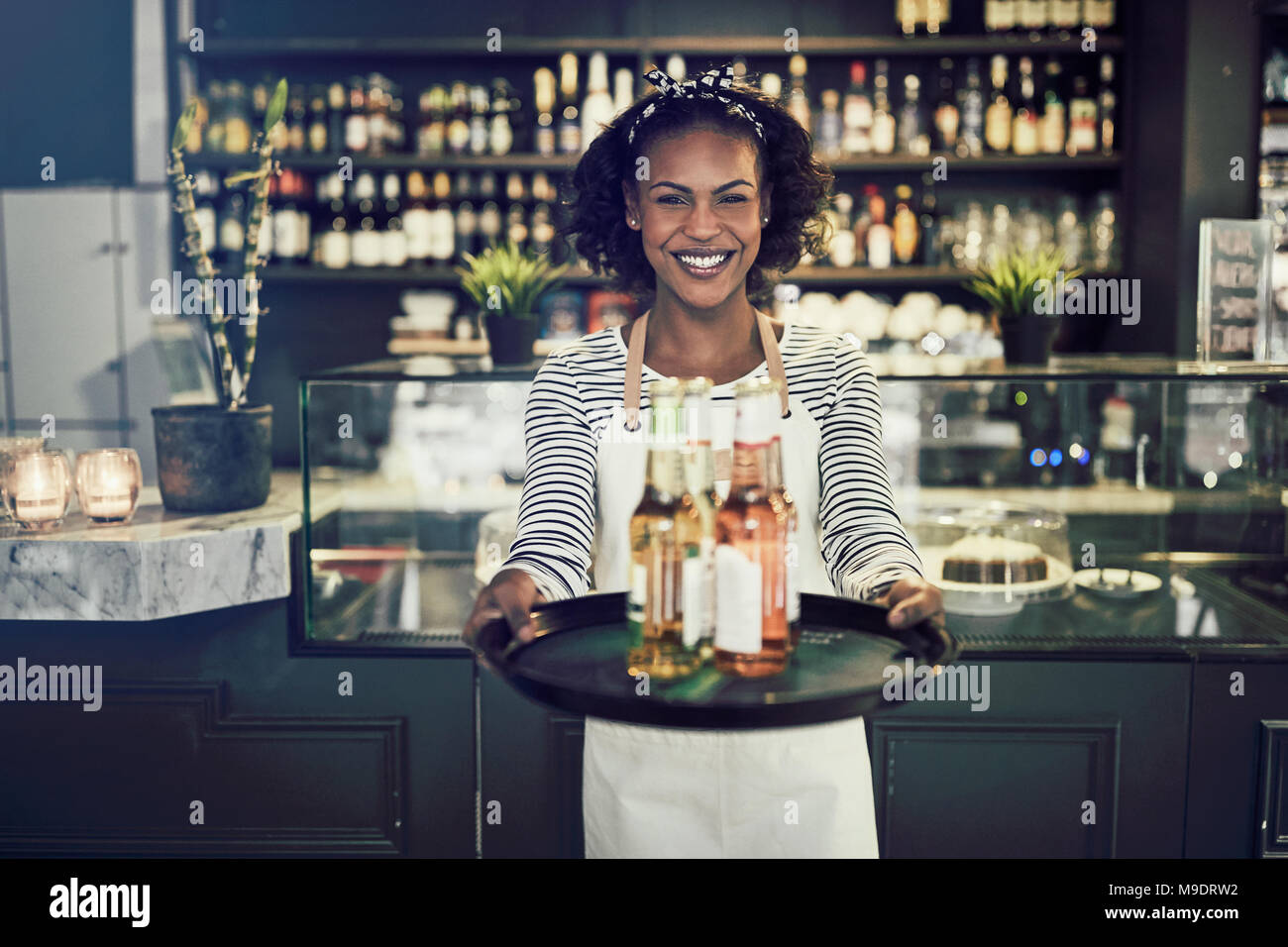 Smiling young African waitress standing in a trendy restaurant holding ...