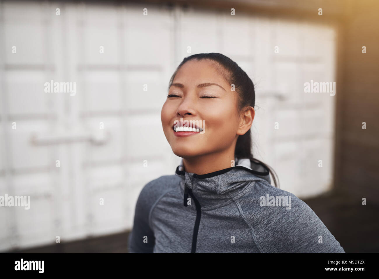 Smiling young Asian woman in jogging clothes standing outside with her ...
