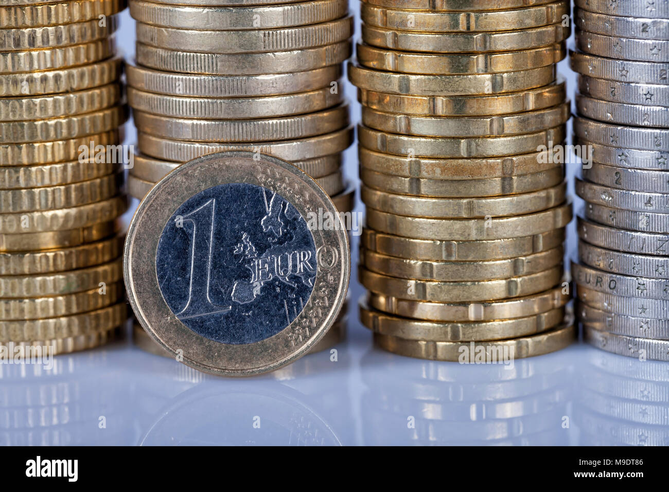 A one euro coin in front of many more coins stacked in columns on white ...
