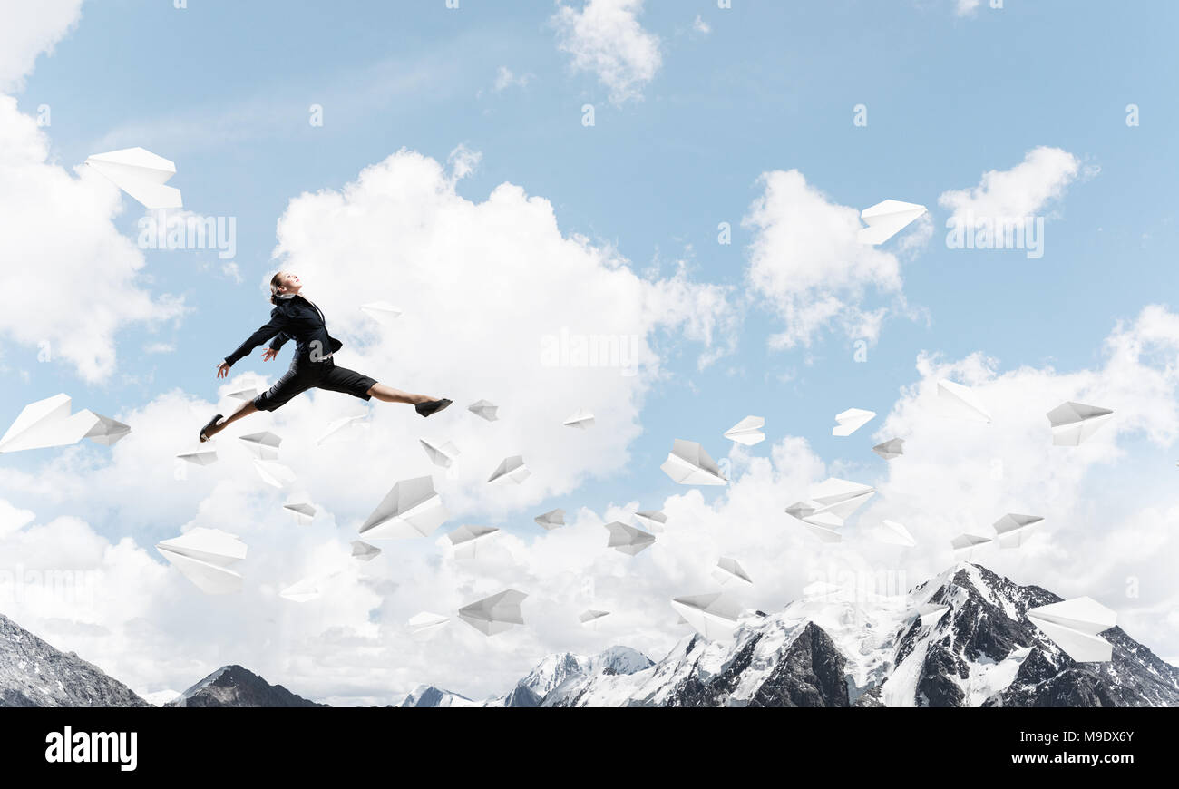 Attractive business woman in suit jumping in the air among flying paper ...