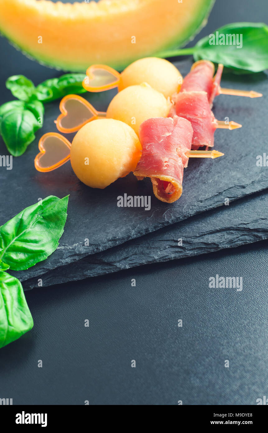 Colorful canape on skewers with melon and prosciutto on a slate plate ...