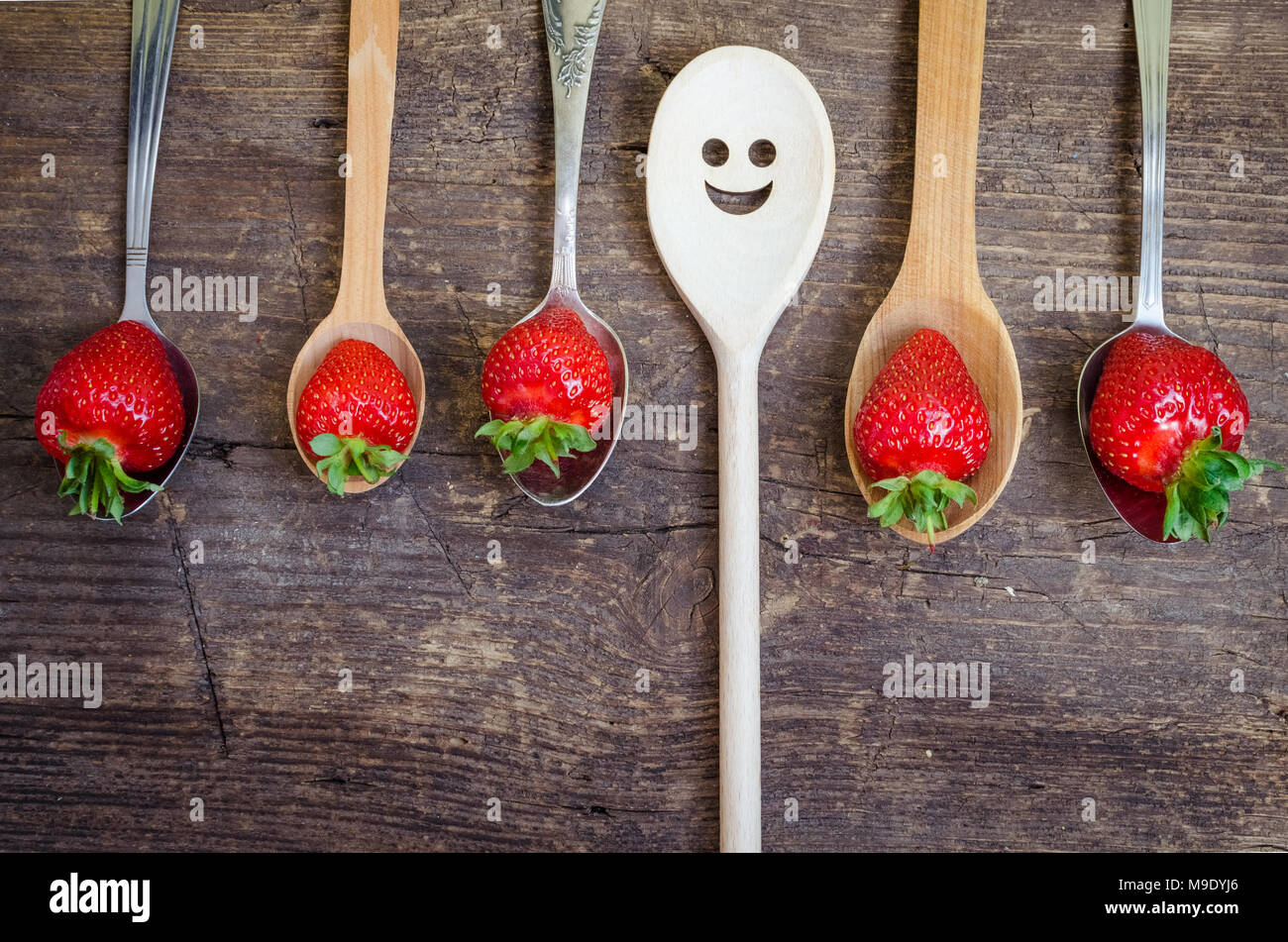 Strawberries on vintage spoons and wooden spoon with smiley face over ...