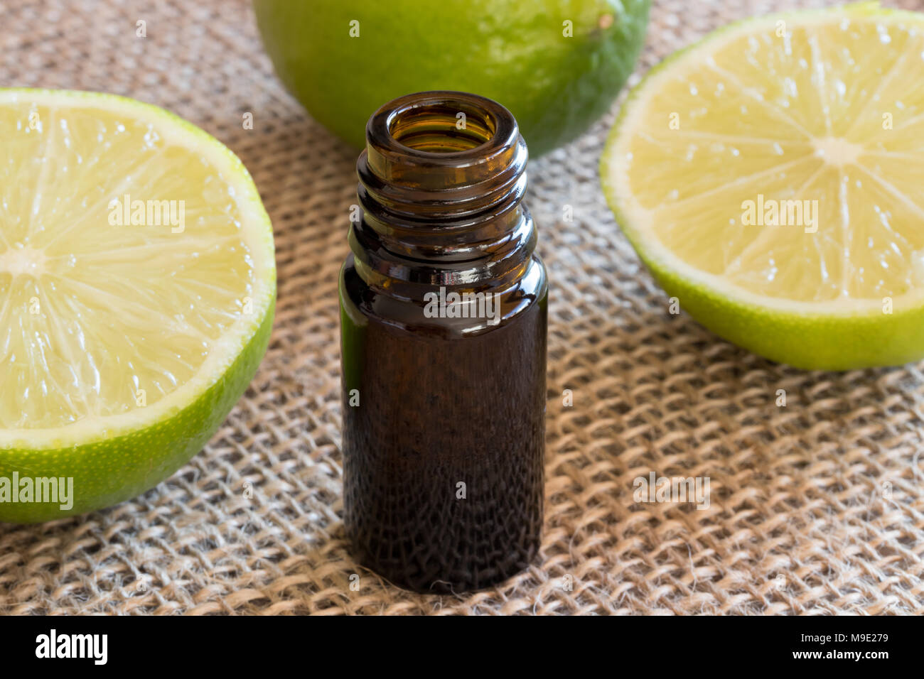 A dark bottle of lime essential oil with fresh limes in the background ...