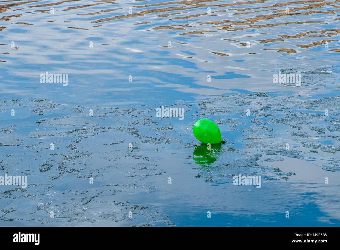 Bright green toy balloon in a cold blue water of a river covered with ...