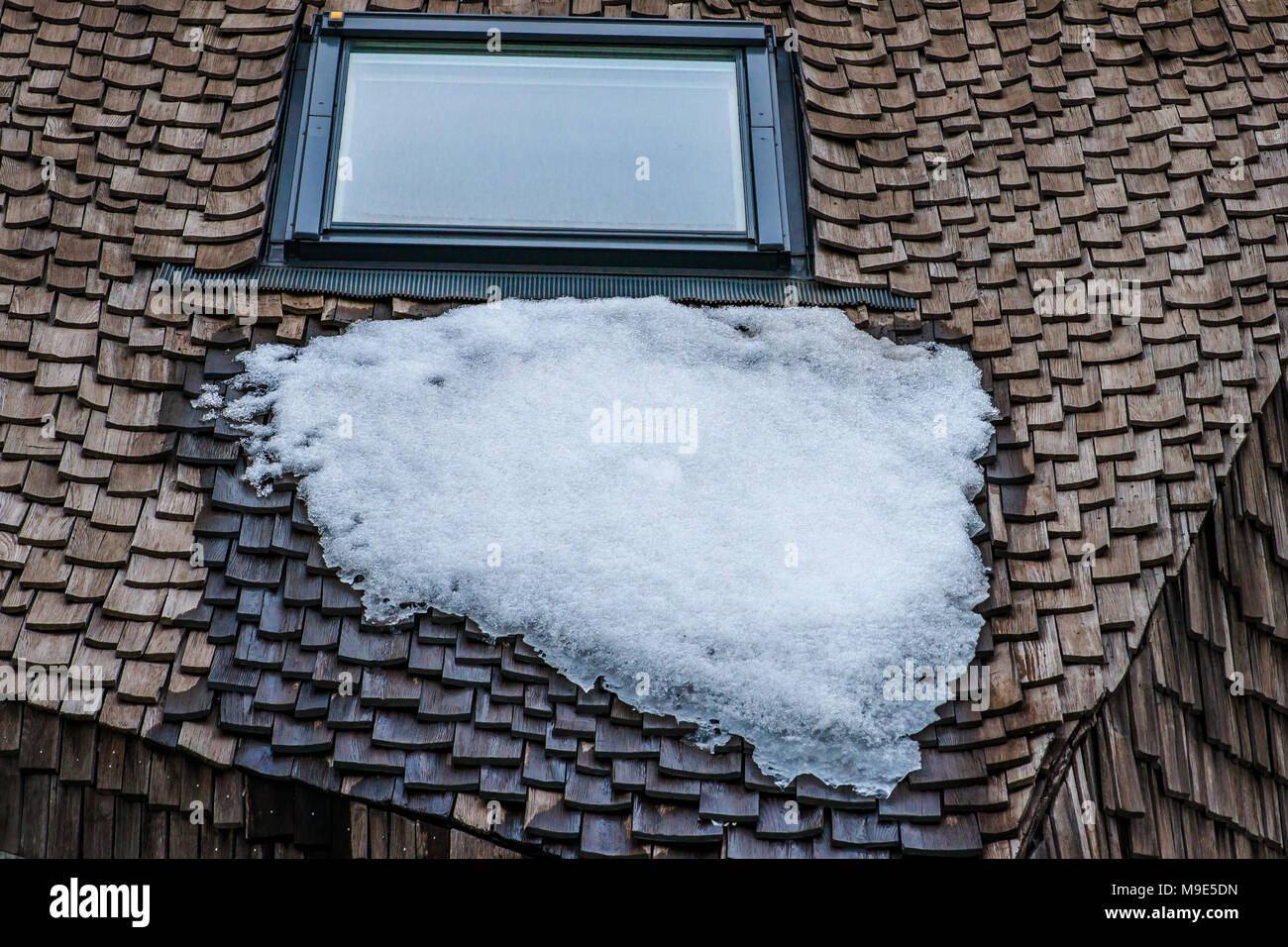 Plate of snow melts under the square window on a decorative wooden roof ...
