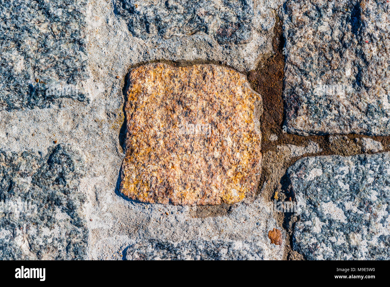 Brown color granite paving block surrounded by grey color stones ...