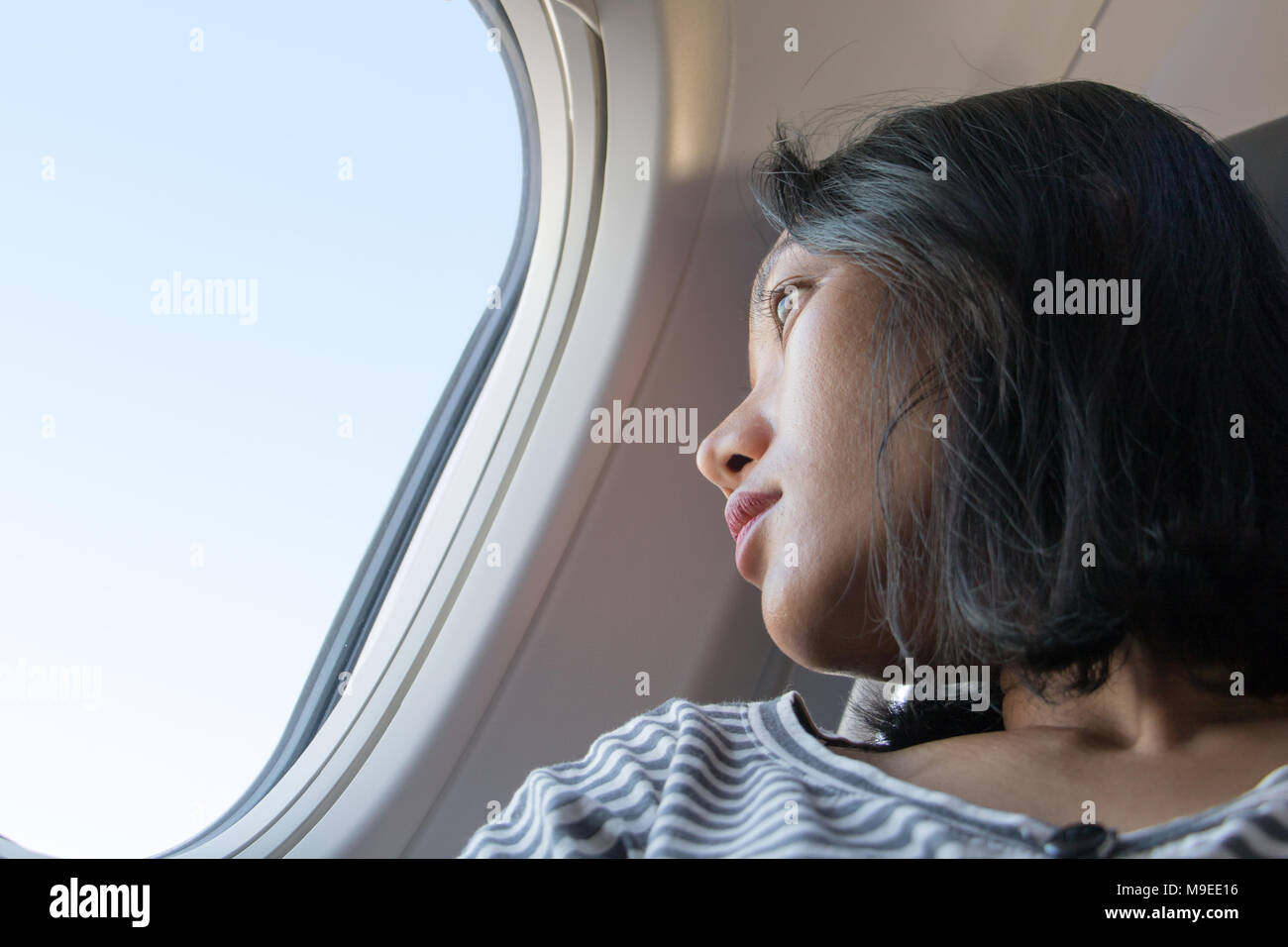 A young woman flying by plane. The passenger is looking out of the ...