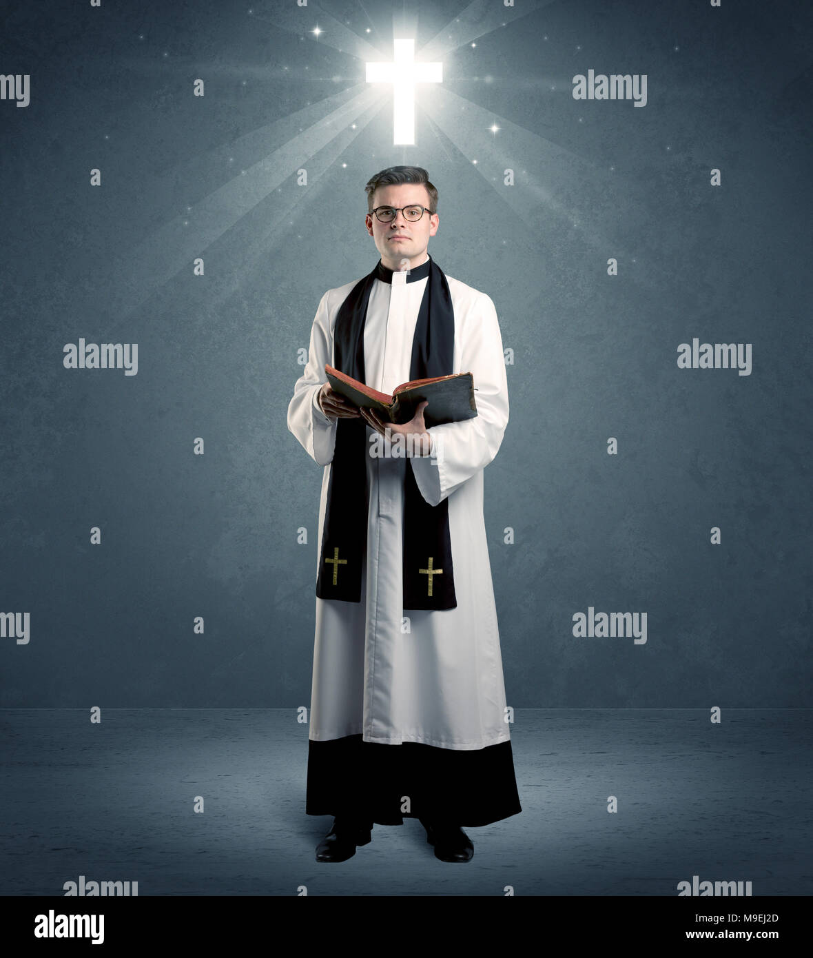 A young caucasian priest with deep faith blessing with the holy bible ...