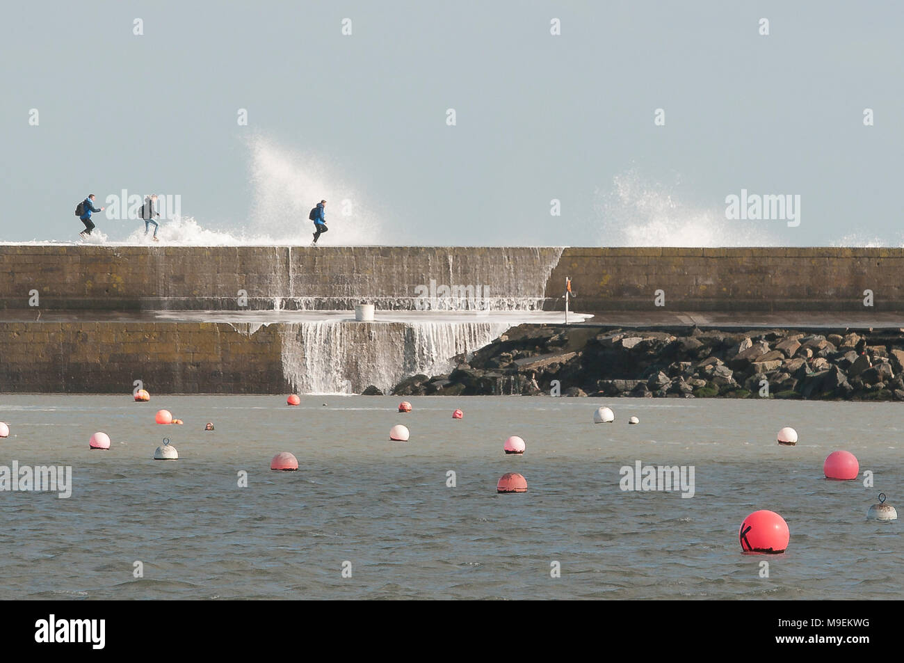 Three young men run along a harbour wall as dangerous waves crash over ...