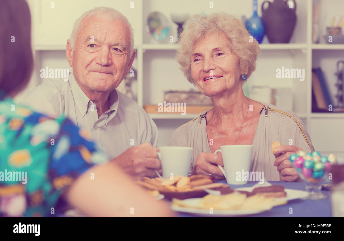 Happy senior couple enjoying conversation with female guest over cup of ...