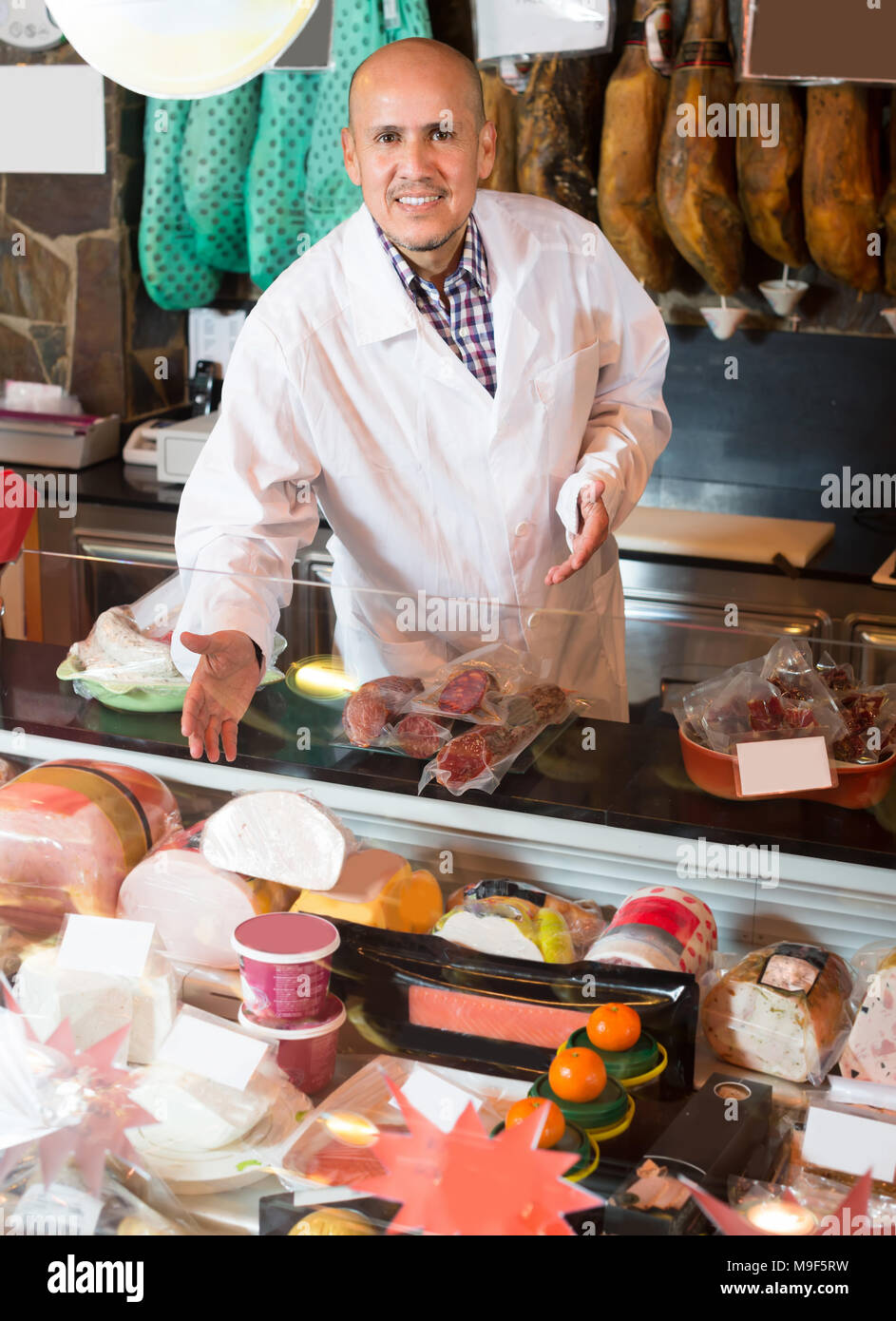 Portrait of positive smiling male seller in white overall offering ...