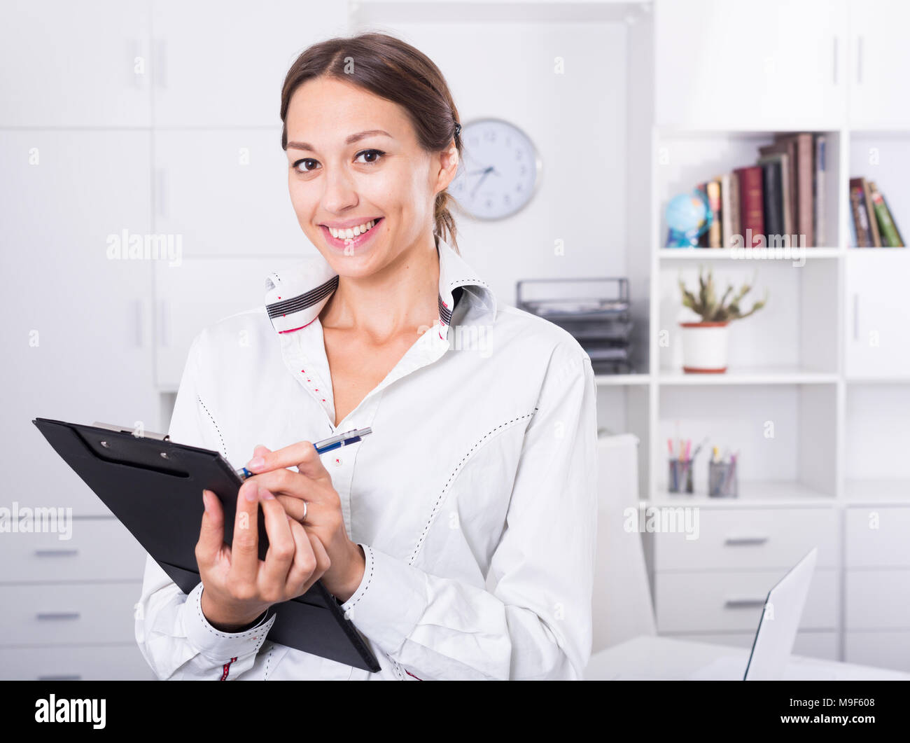 smiling business female employee holding clipboard in hands in firm ...
